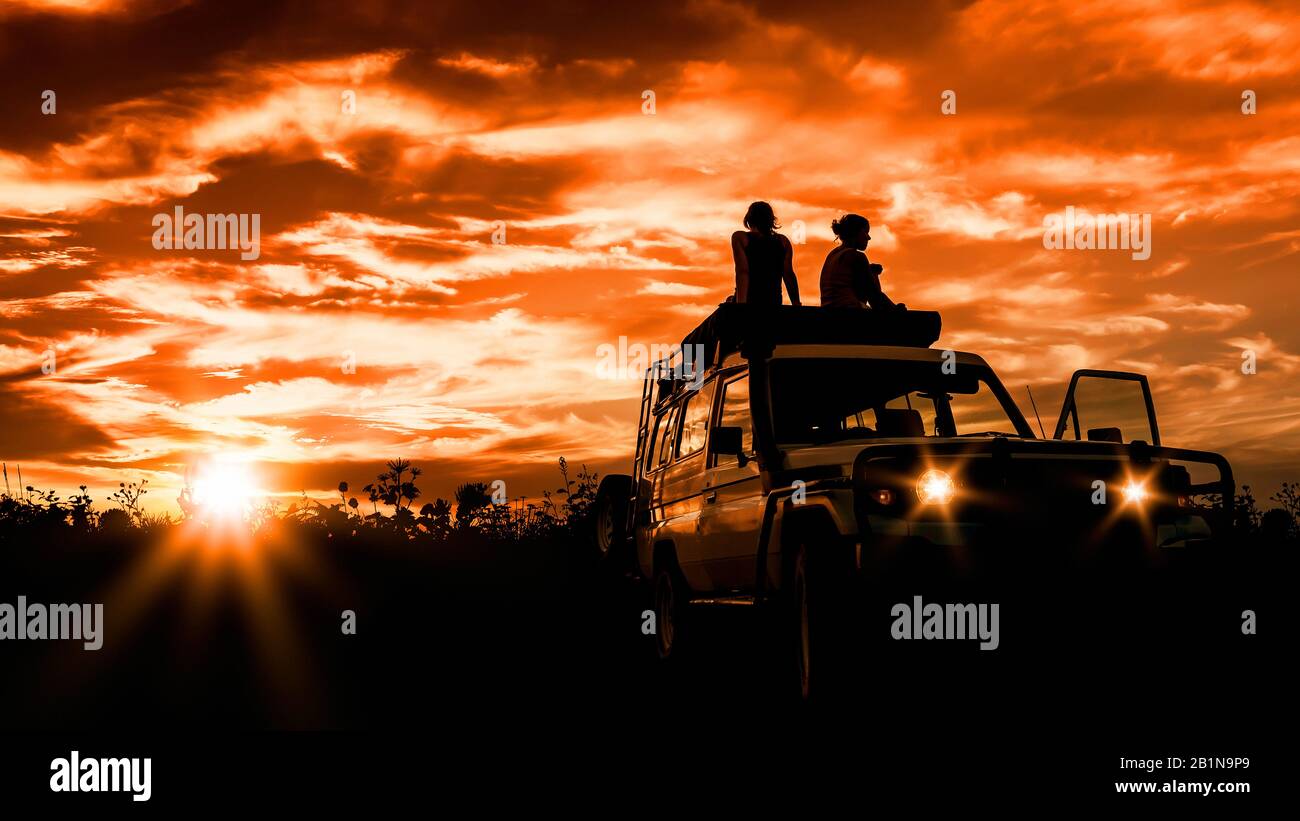 two women sit on their jeep enjoying the sunset over the outback ...