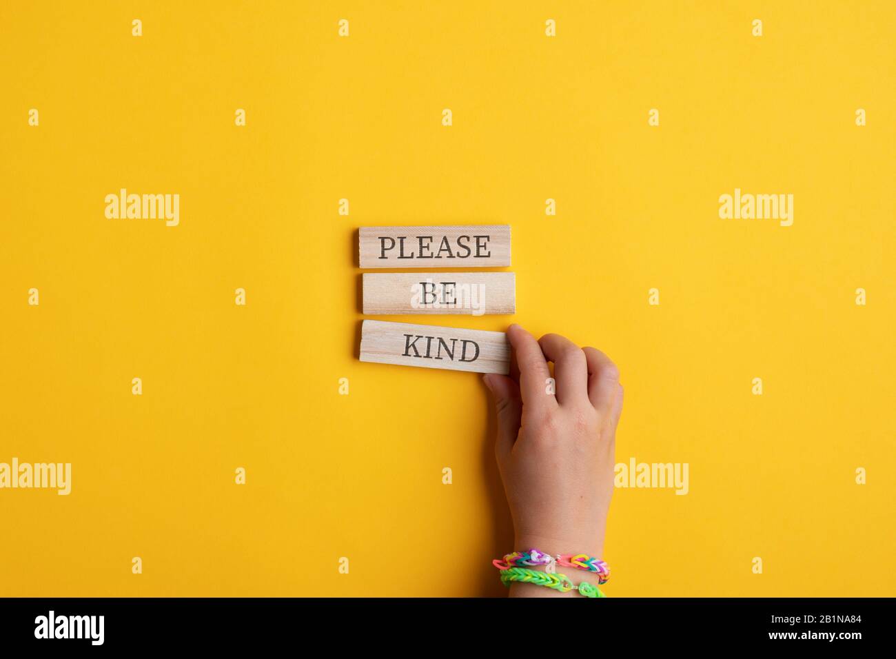 Hand of a child making a Please be kind sign written on wooden pegs ...