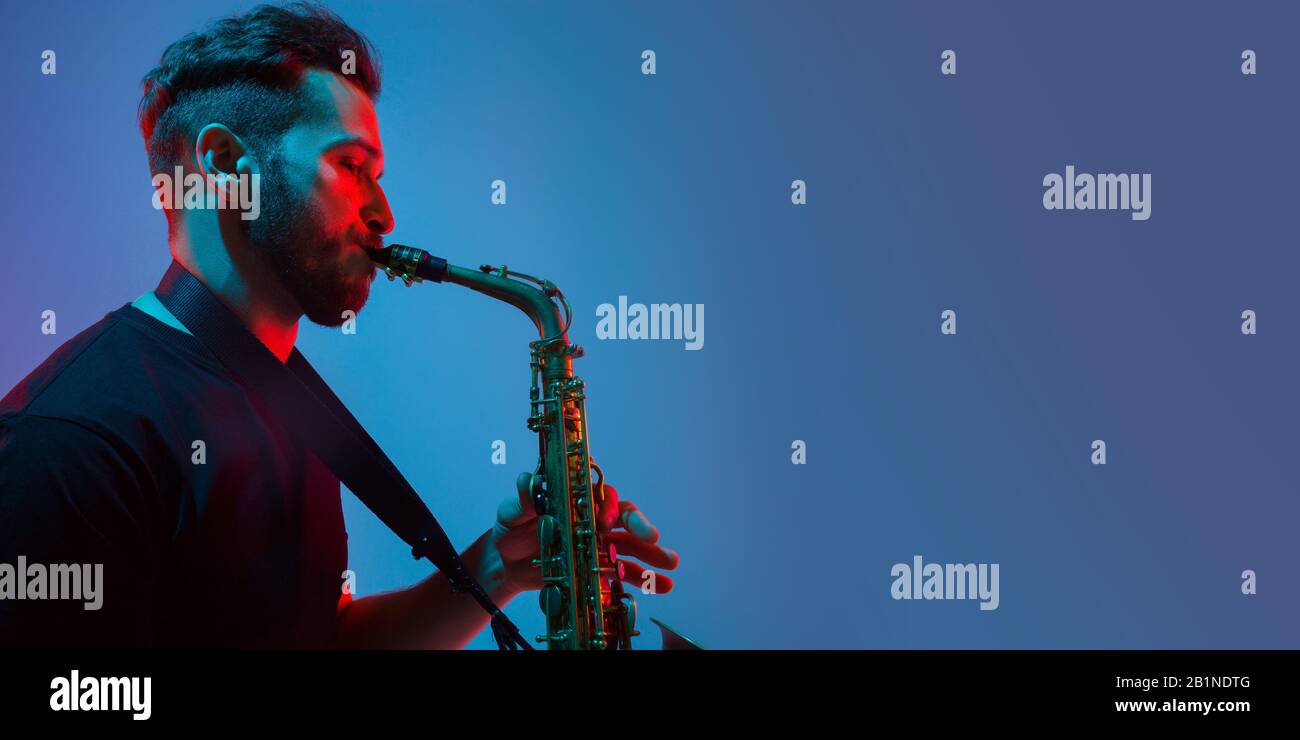 Young caucasian jazz musician playing the saxophone on gradient blue ...