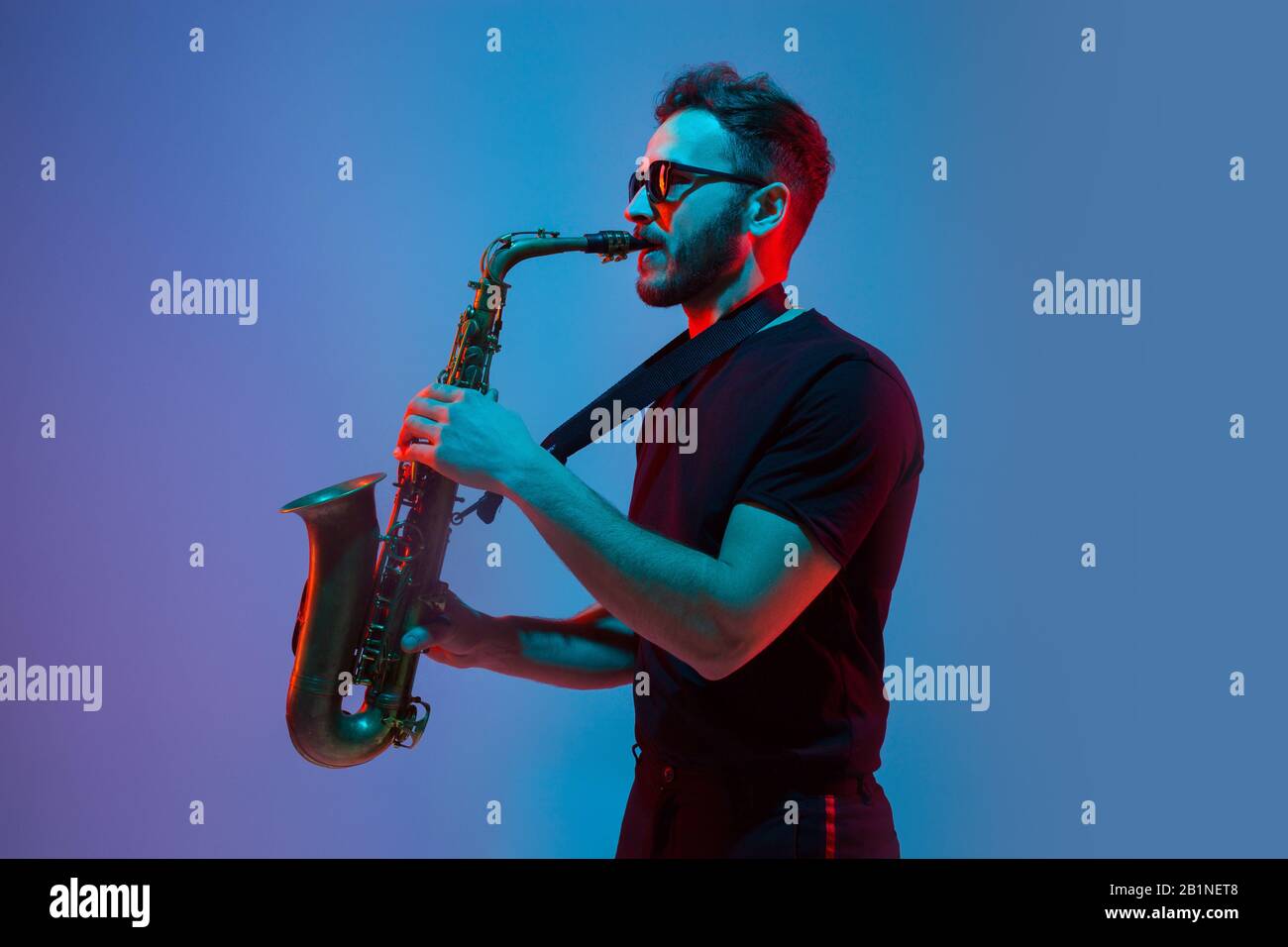Young caucasian jazz musician playing the saxophone on gradient blue ...