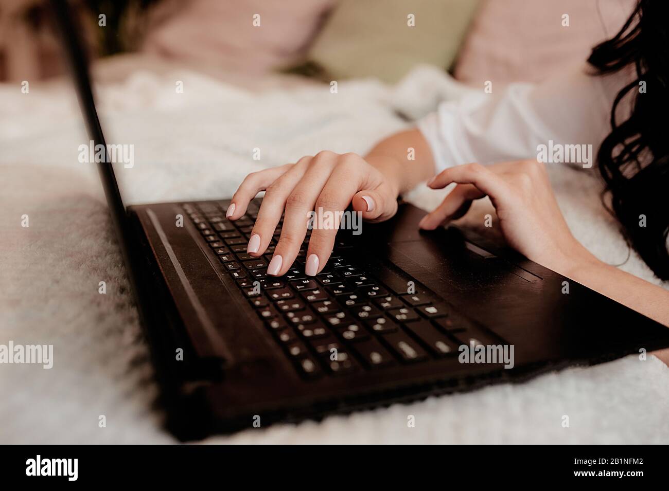 a woman's hand with a neat pink manicure is typing on a laptop keyboard ...