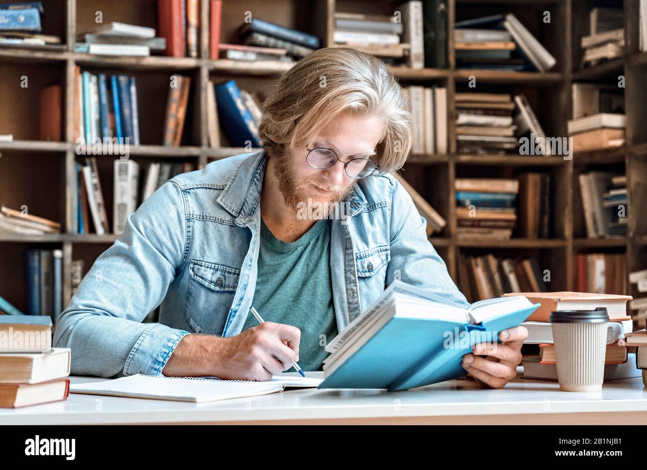 Focused young man in glasses sit library desk make notes education ...