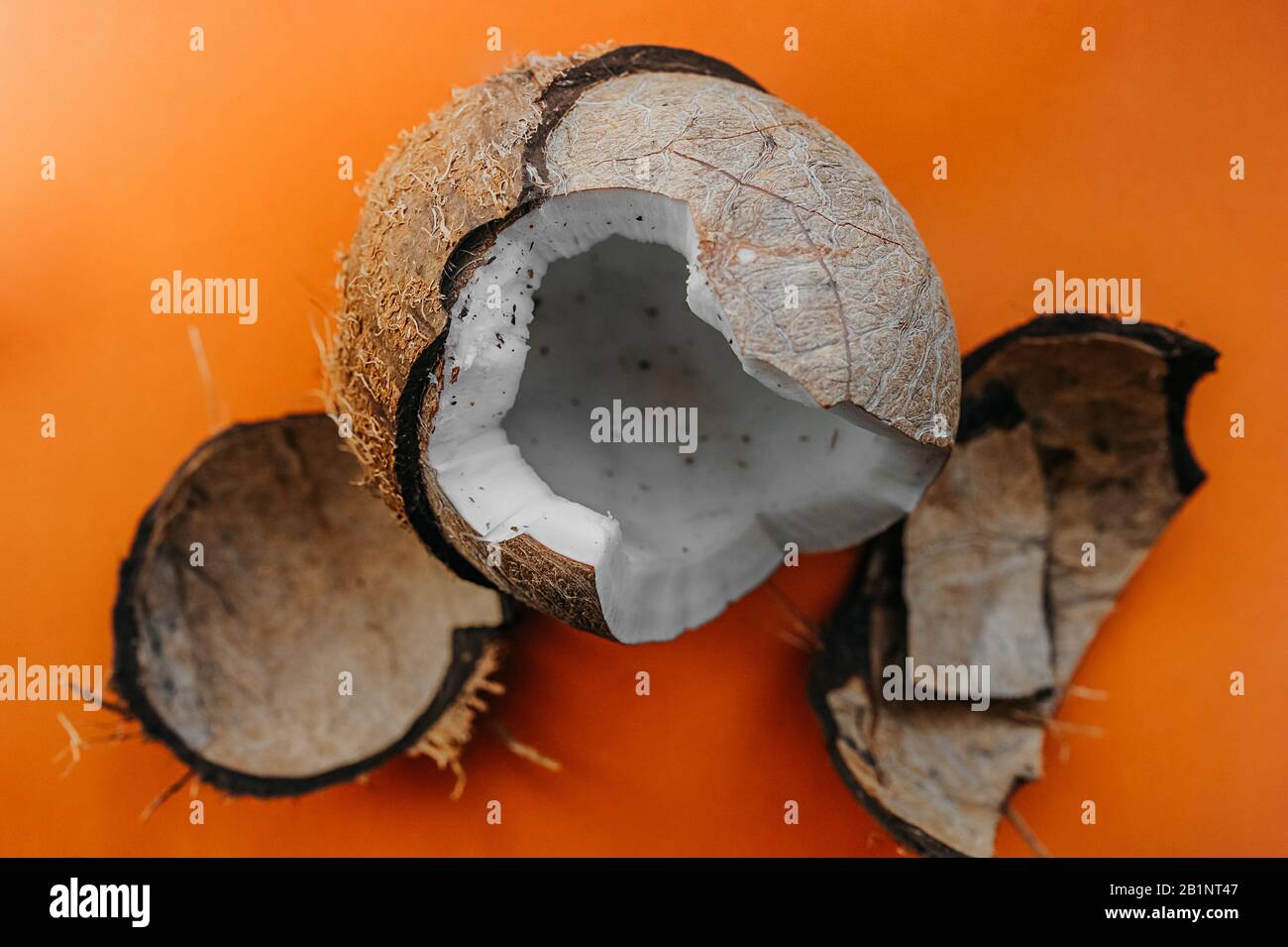 Broken ripe coconut with juicy pulp on a bright orange plain background ...