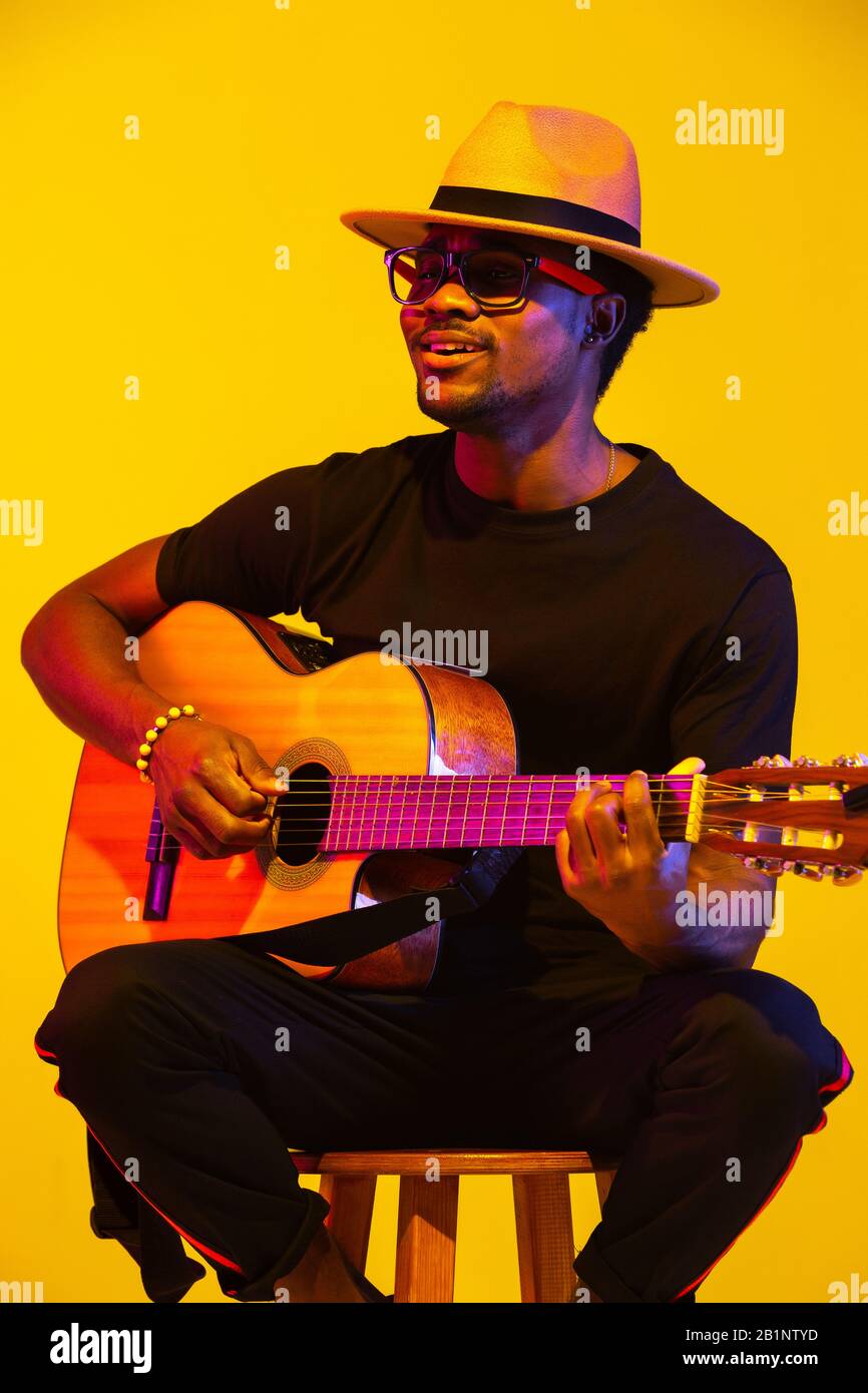 Young and joyful african-american musician playing guitar and singing ...