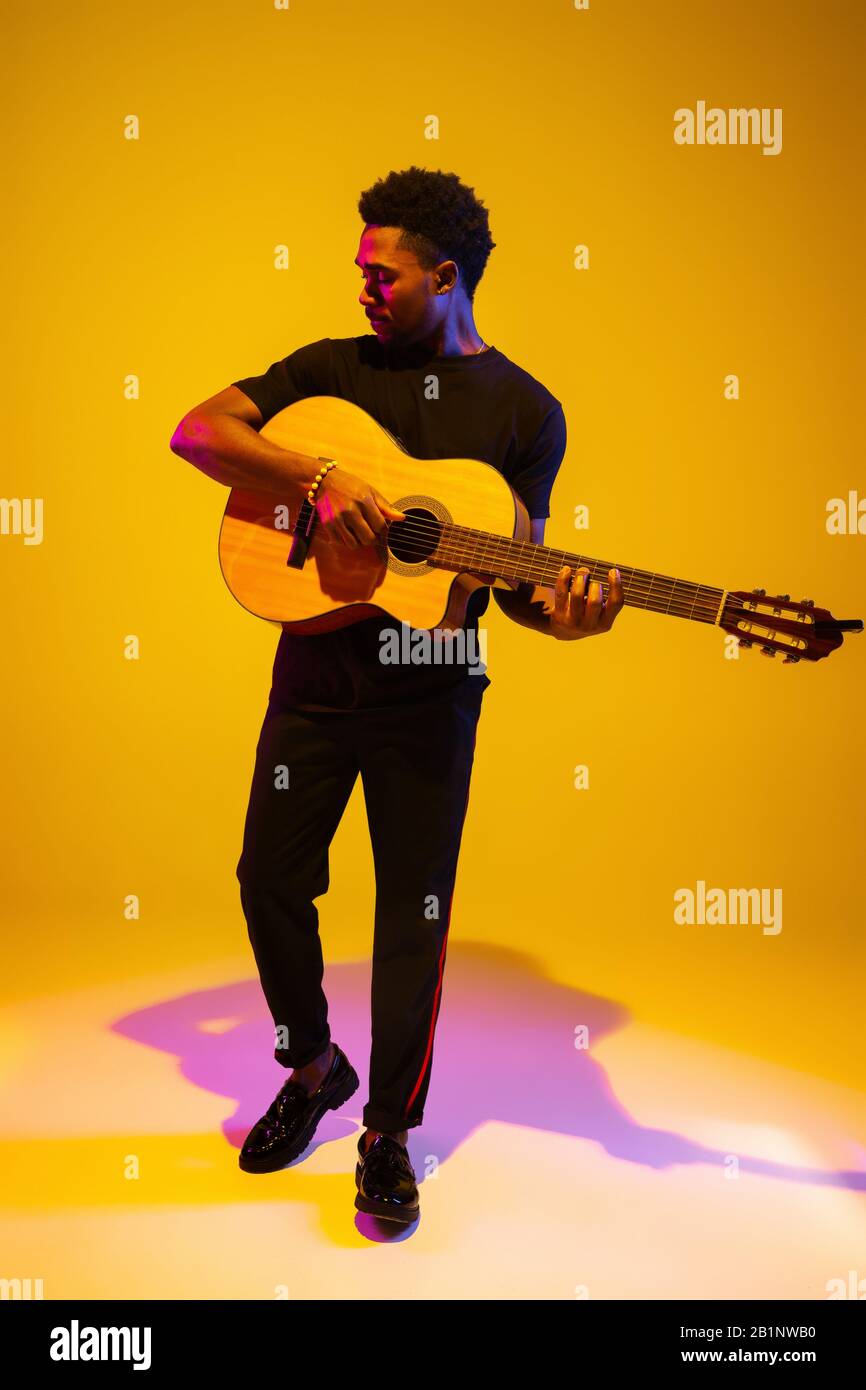 Young and joyful african-american musician playing guitar and singing ...
