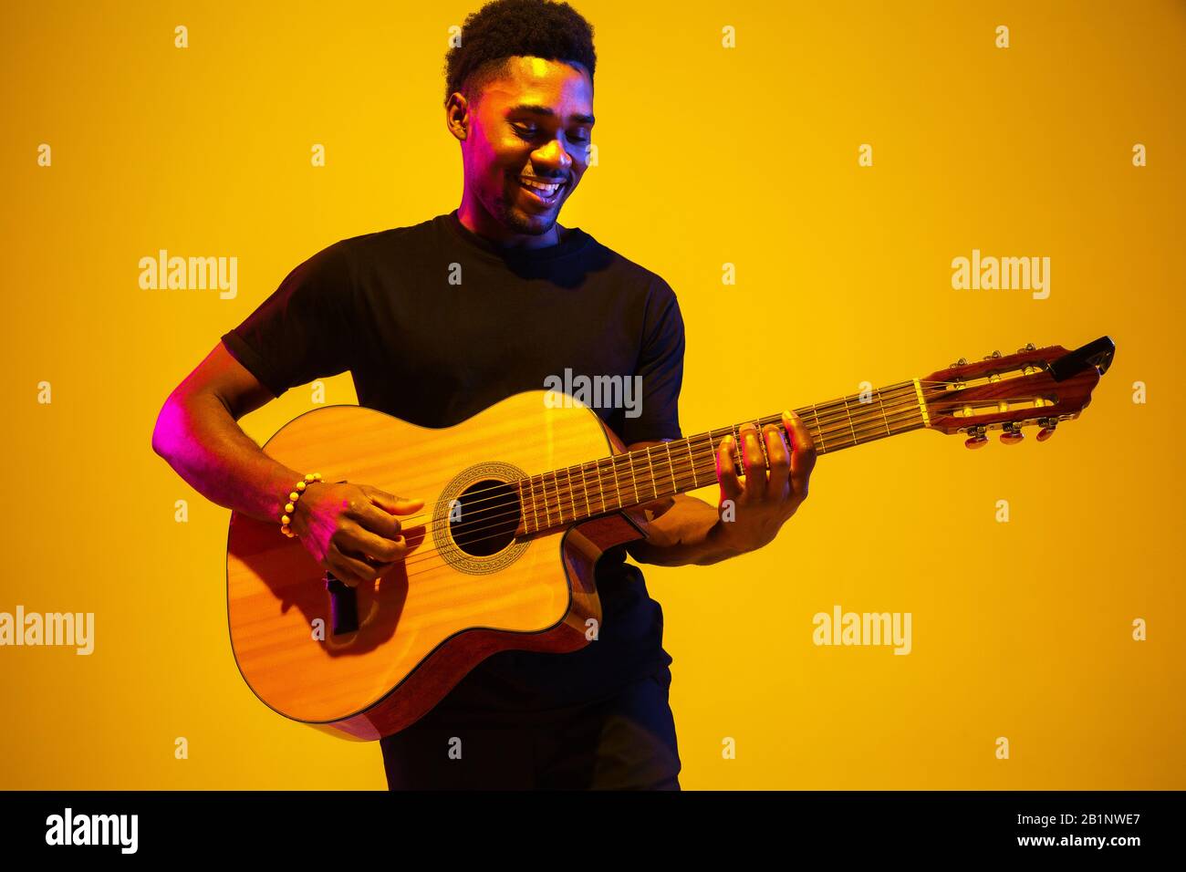 Young and joyful african-american musician playing guitar and singing ...