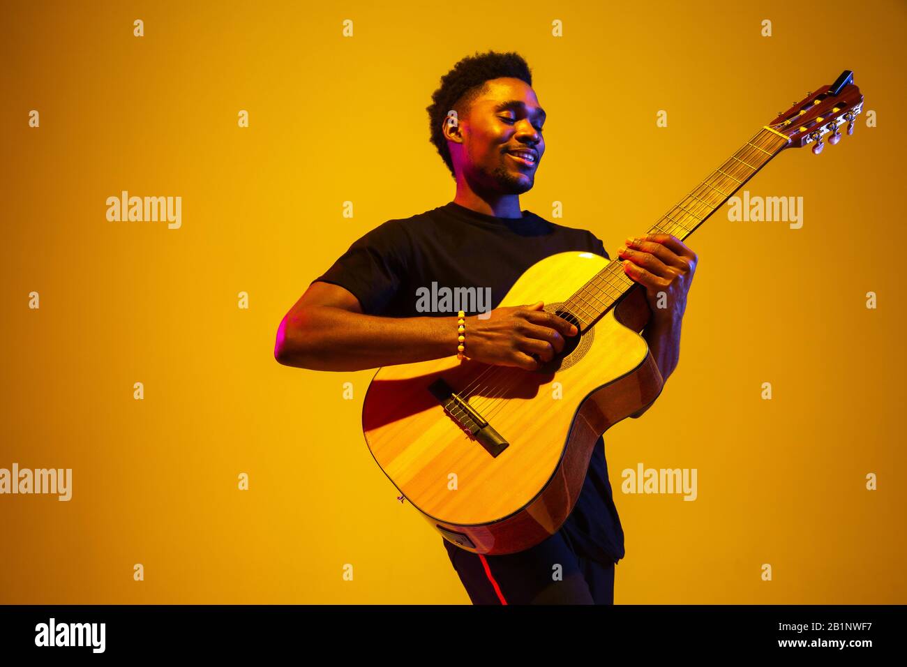 Young and joyful african-american musician playing guitar and singing ...