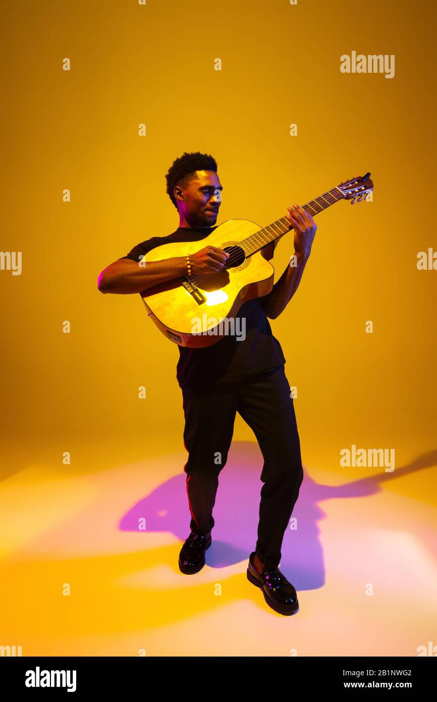 Young and joyful african-american musician playing guitar and singing ...