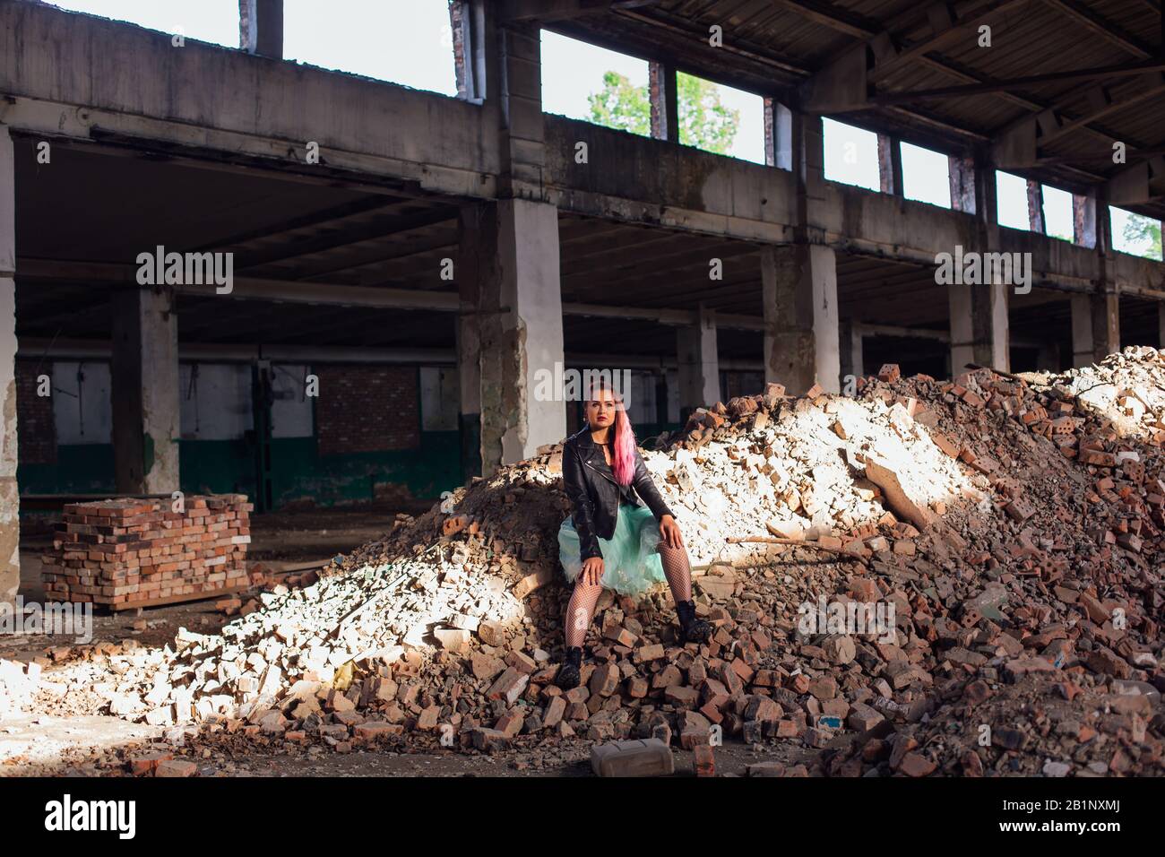 Young girl with pink hair sitting on bricks in a collapsed building ...