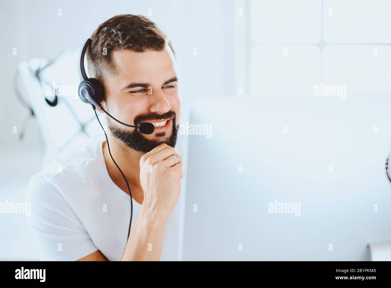 Young smiling customer support operator with hands-free headset working ...