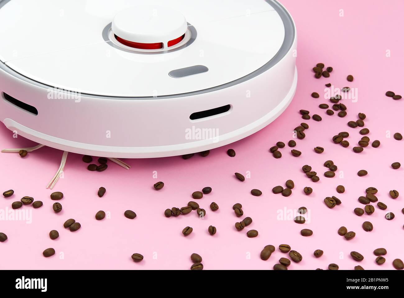 white robot vacuum cleaner on a pink background with coffee grains ...