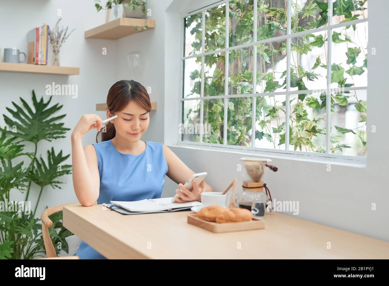 Young Asian woman writing in the notebook and using phone while sitting ...