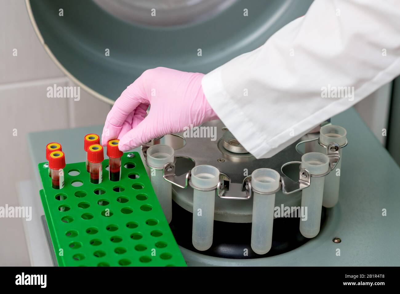 Doctor taking specimen tube of blood from tray to centrifuge machine in ...