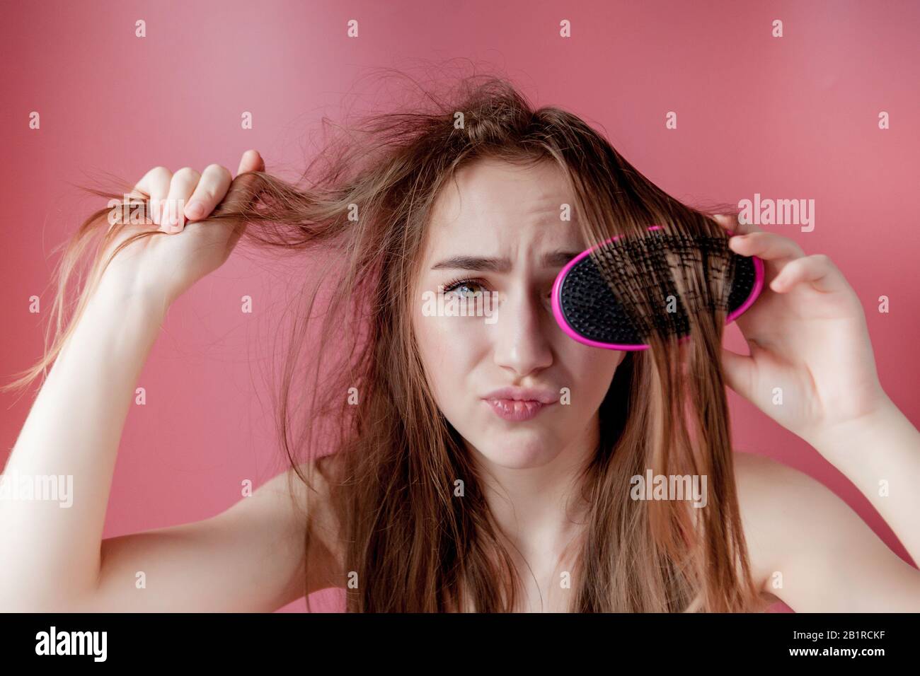 Young beautiful girl having problems while hair on pink background ...