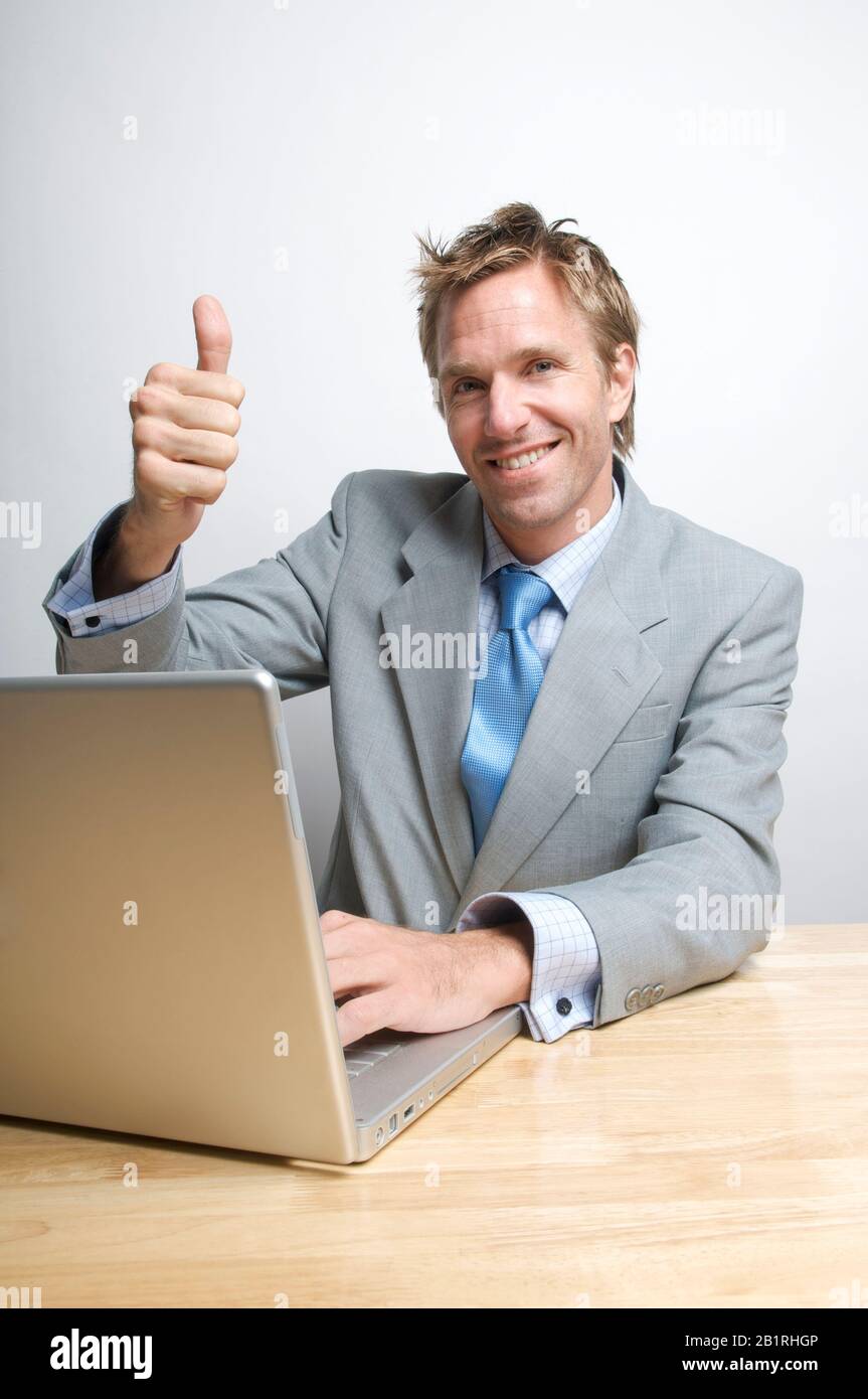 Happy businessman giving the camera a thumbs up sitting at his desk in ...