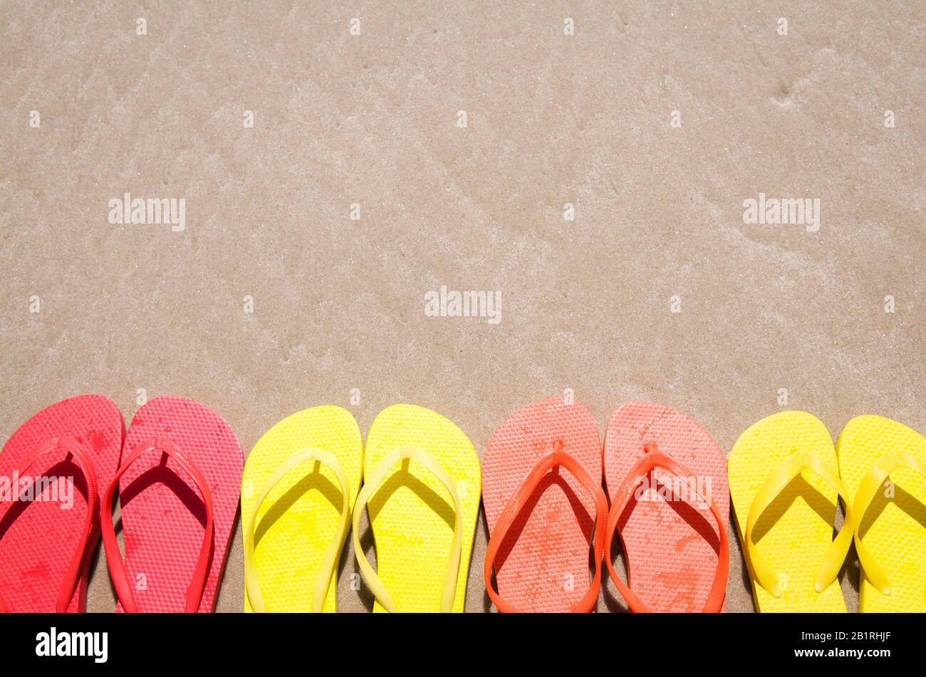 Group of flip-flops in bright summer colors lined up on smooth sand ...