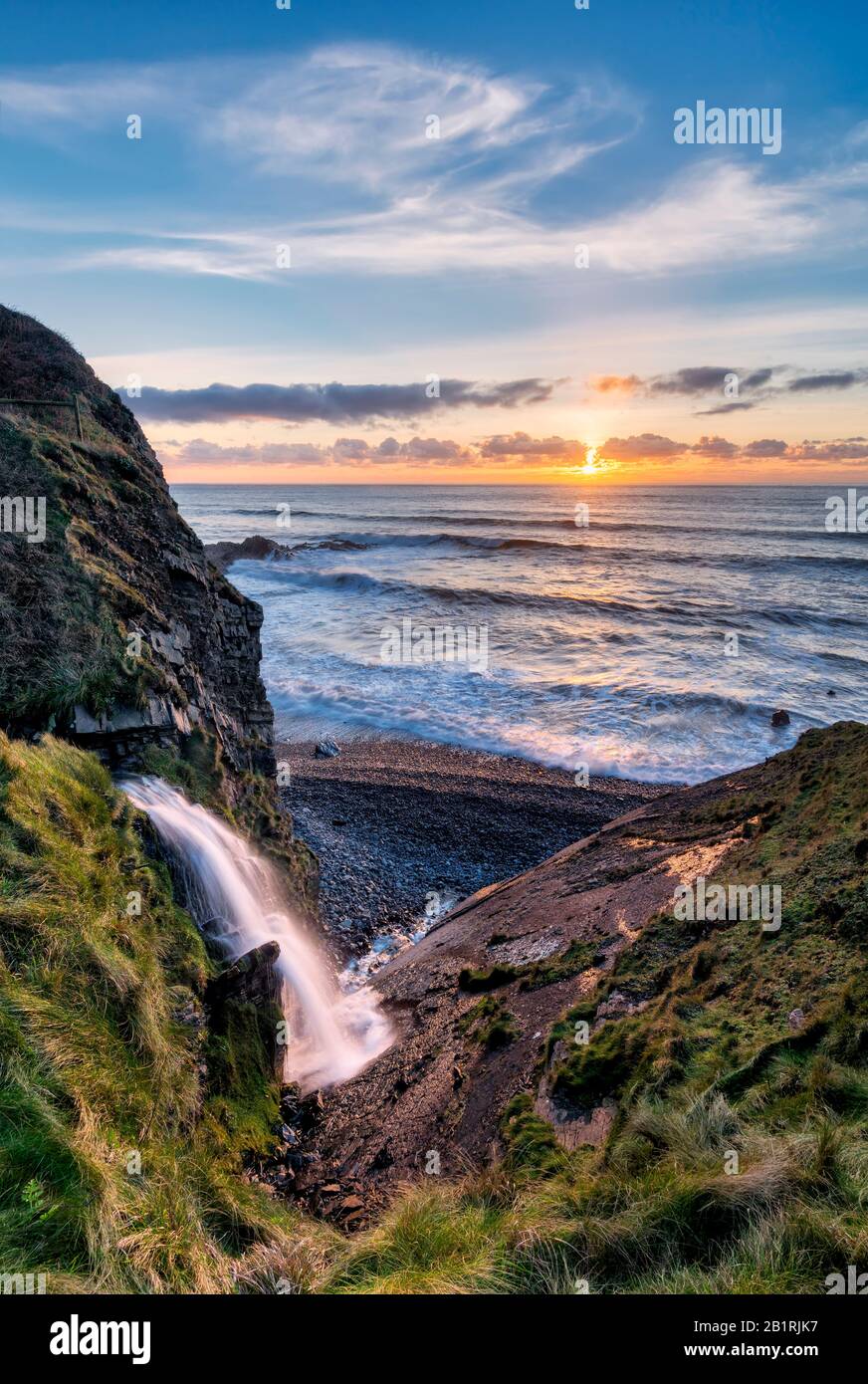 Waterfall cascading over the rocks with views to sea with the sun ...