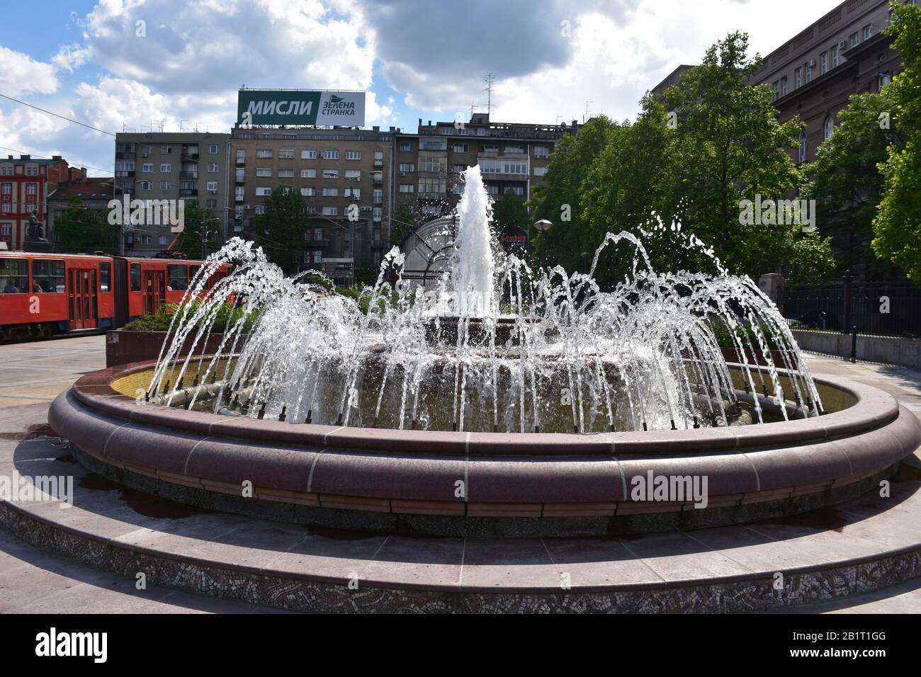 Round town fountain in the square with tall buildings in the background ...
