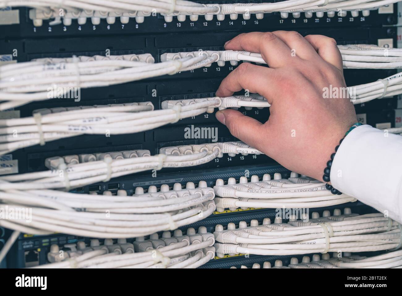 man working in network server room with fiber optic hub for digital ...