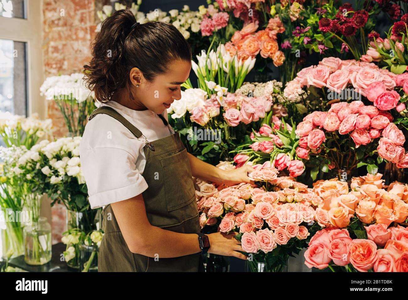 Woman florist wearing apron looking on flowers in her store Stock Photo ...