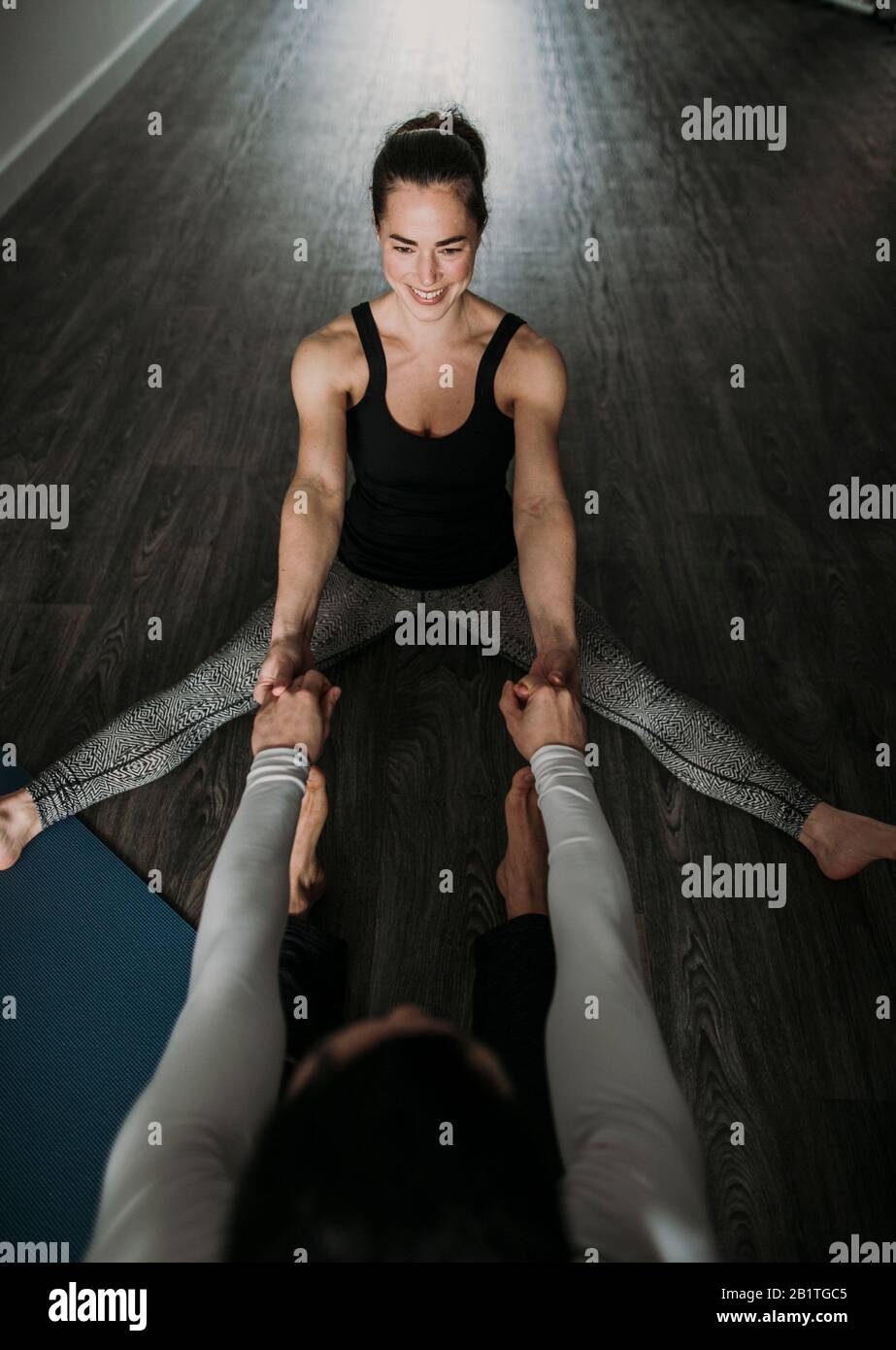 smiling female personal trainer helps client stretch by holding hands ...