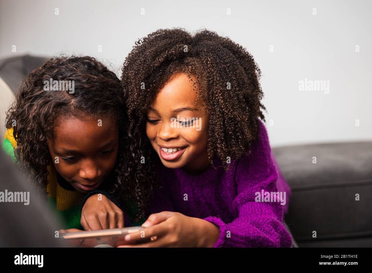 Smiling sisters using mobile phone at home Stock Photo - Alamy