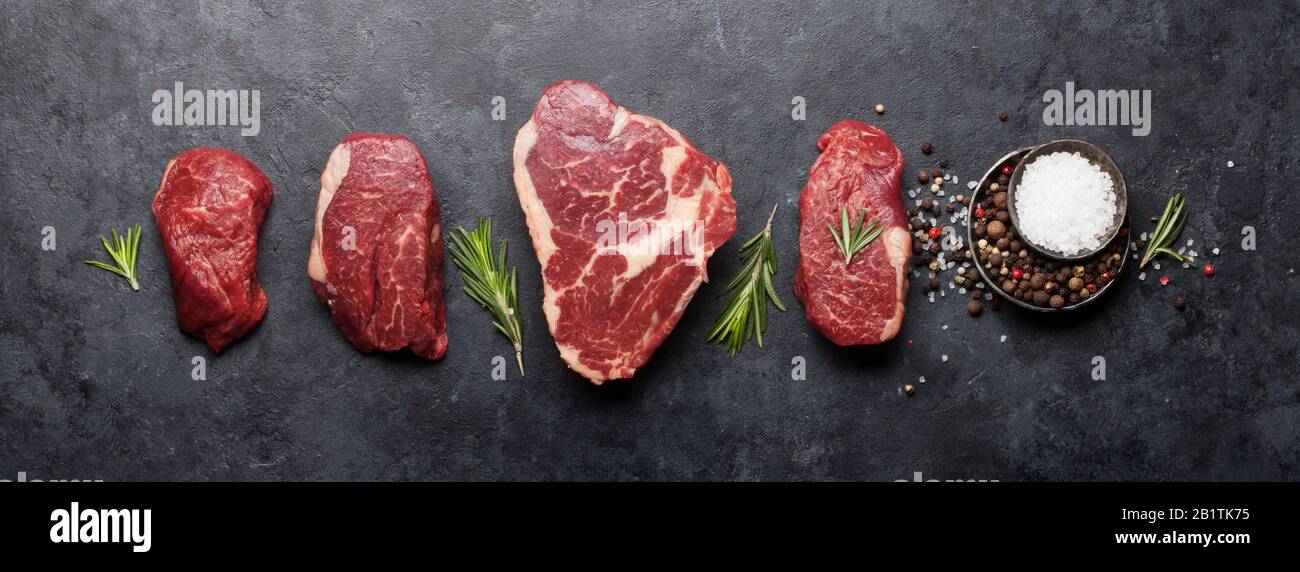Variety of fresh raw beef steaks with spices on stone table. Top view ...