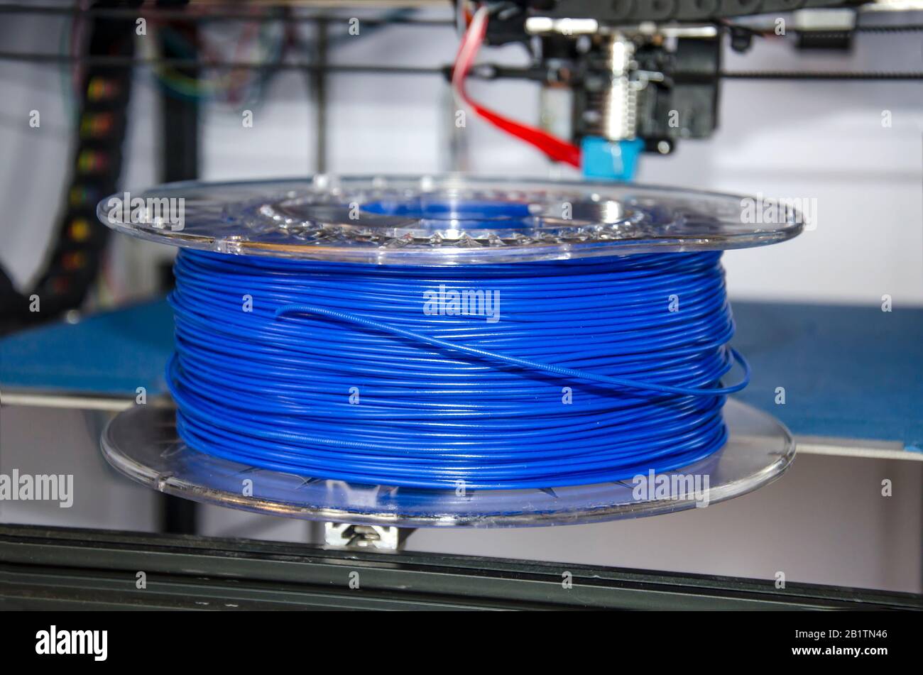 View of coil of blue plastic for 3D printing on printer background ...
