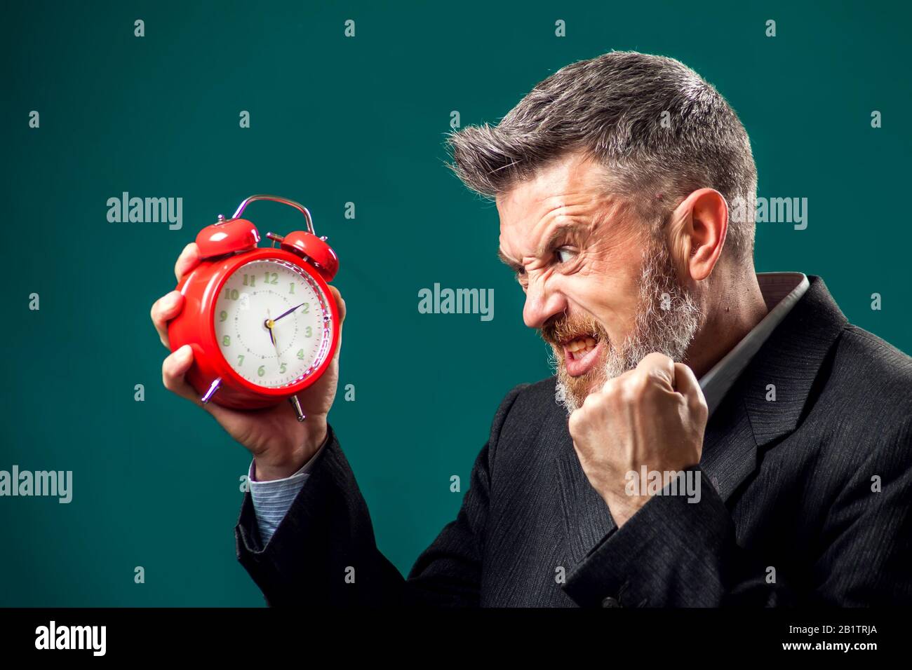 Angry bearded businessman in suit holding red alarm clock, shouting and ...