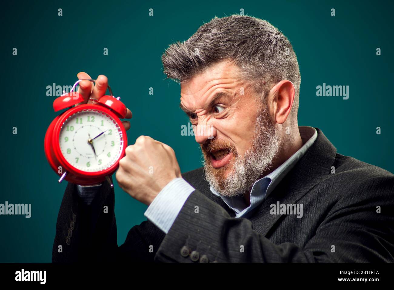 Angry Bearded Businessman In Suit Holding Red Alarm Clock And Shouting