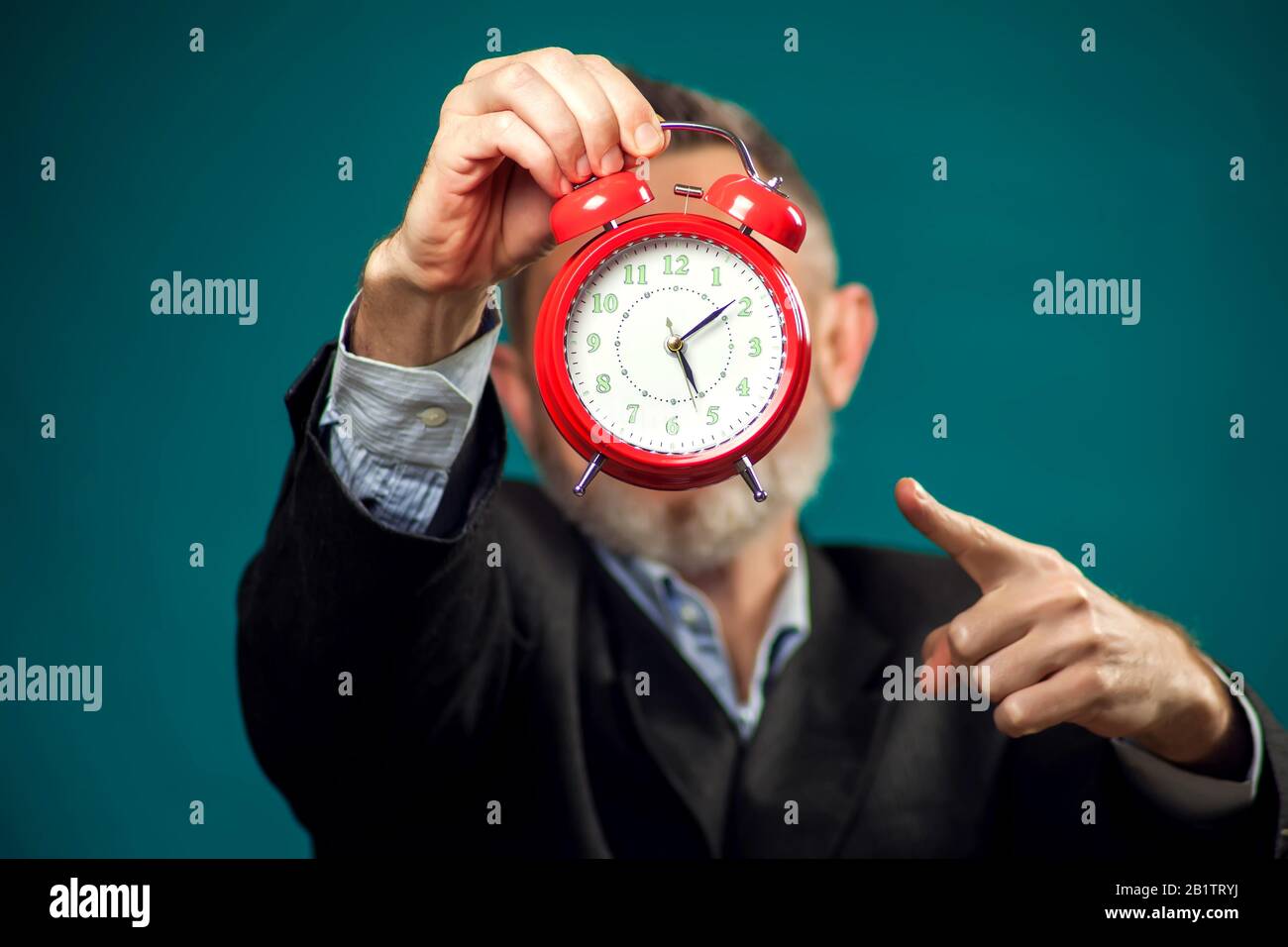 Bearded Businessman In Suit Holding Red Alarm Clock And Pointing With A