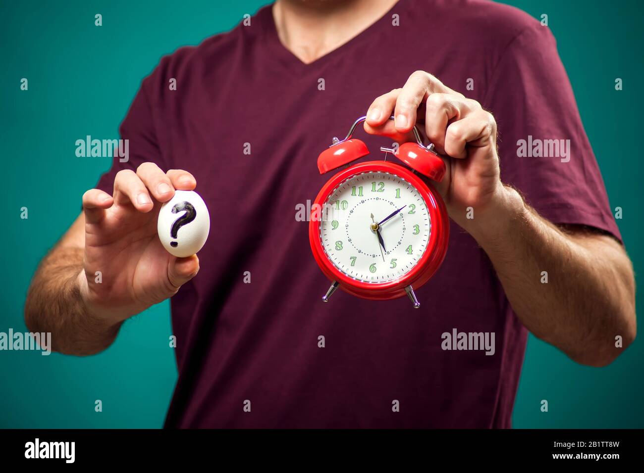 Man in red t-shirt holding egg and alarm clock. Eggs cooking Stock ...
