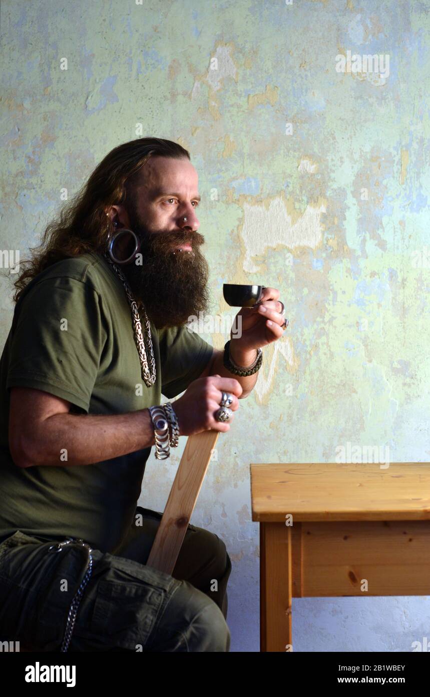 Male with long open hairs and beard sitting on a table with a cup the ...