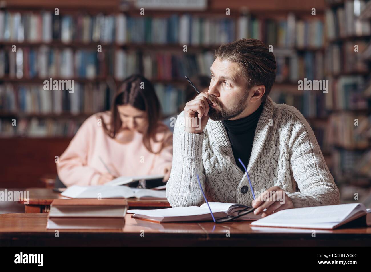 Bearded male reader in casual clothing and eyeglasses sitting at table ...