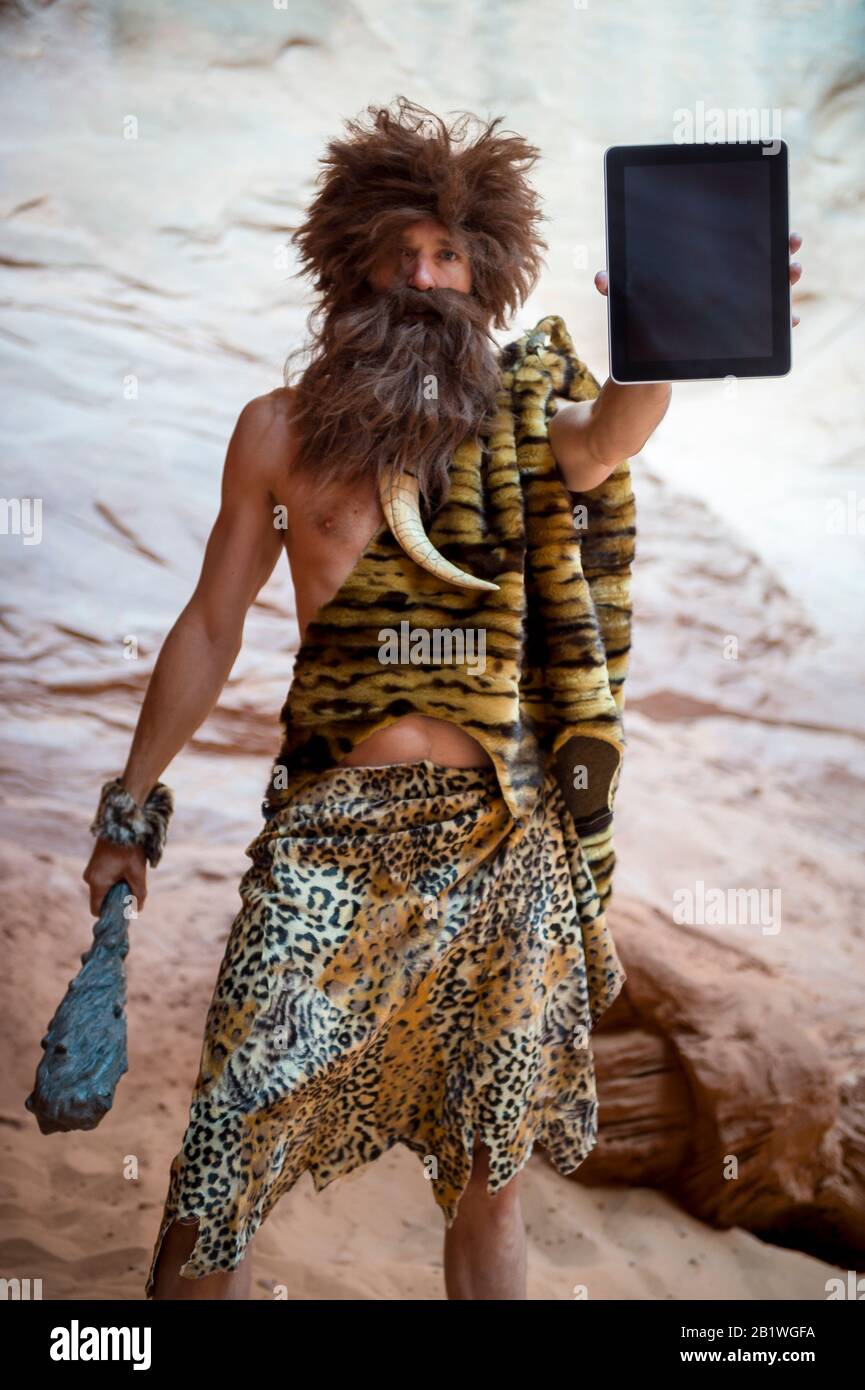 Modern caveman holding the blank screen of a tablet outdoors in a ...
