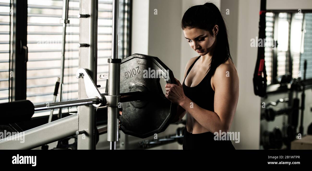 Woman adding weight on a bar as she workout in fitness gym Stock Photo ...