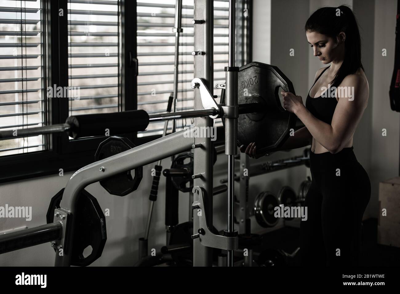 Woman adding weight on a bar as she workout in fitness gym Stock Photo ...