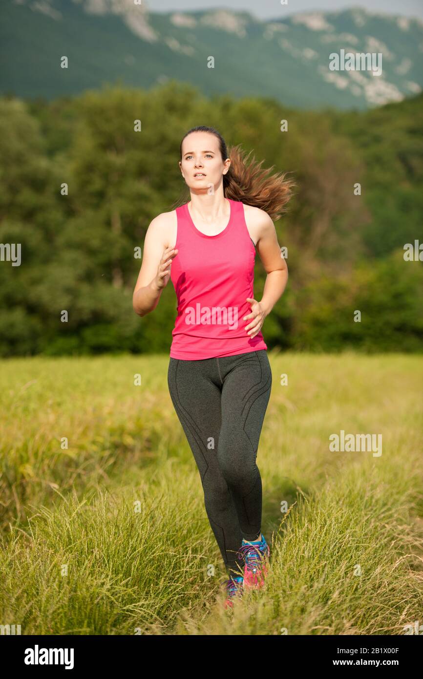 Beautiful young woman workout outdoor runs across meadow in early ...