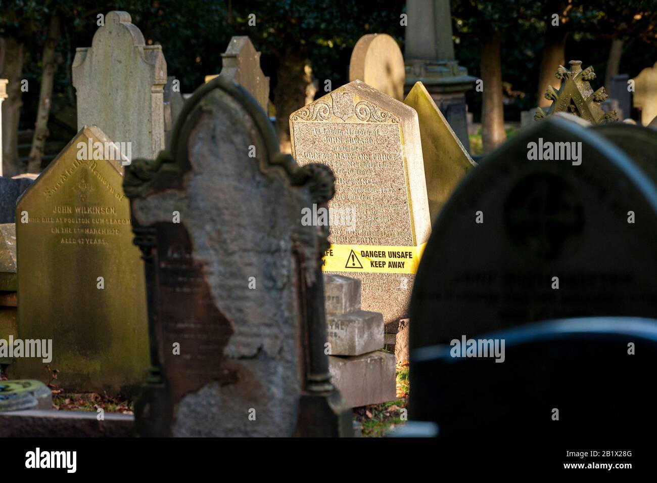 An unsafe gravestone with yellow warning tape around. The tape is ...