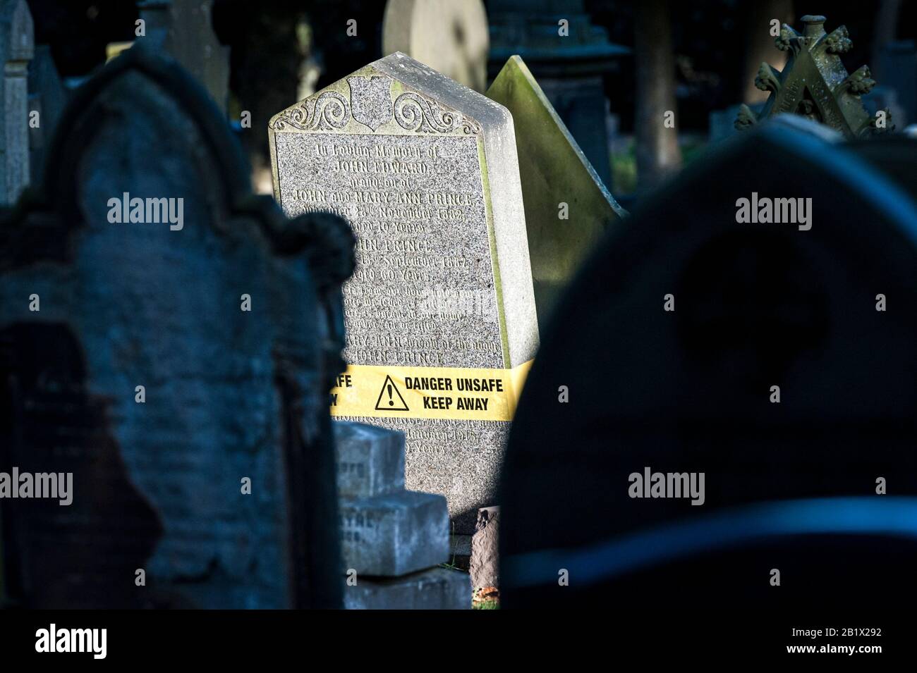 An unsafe gravestone with yellow warning tape around. The tape is ...