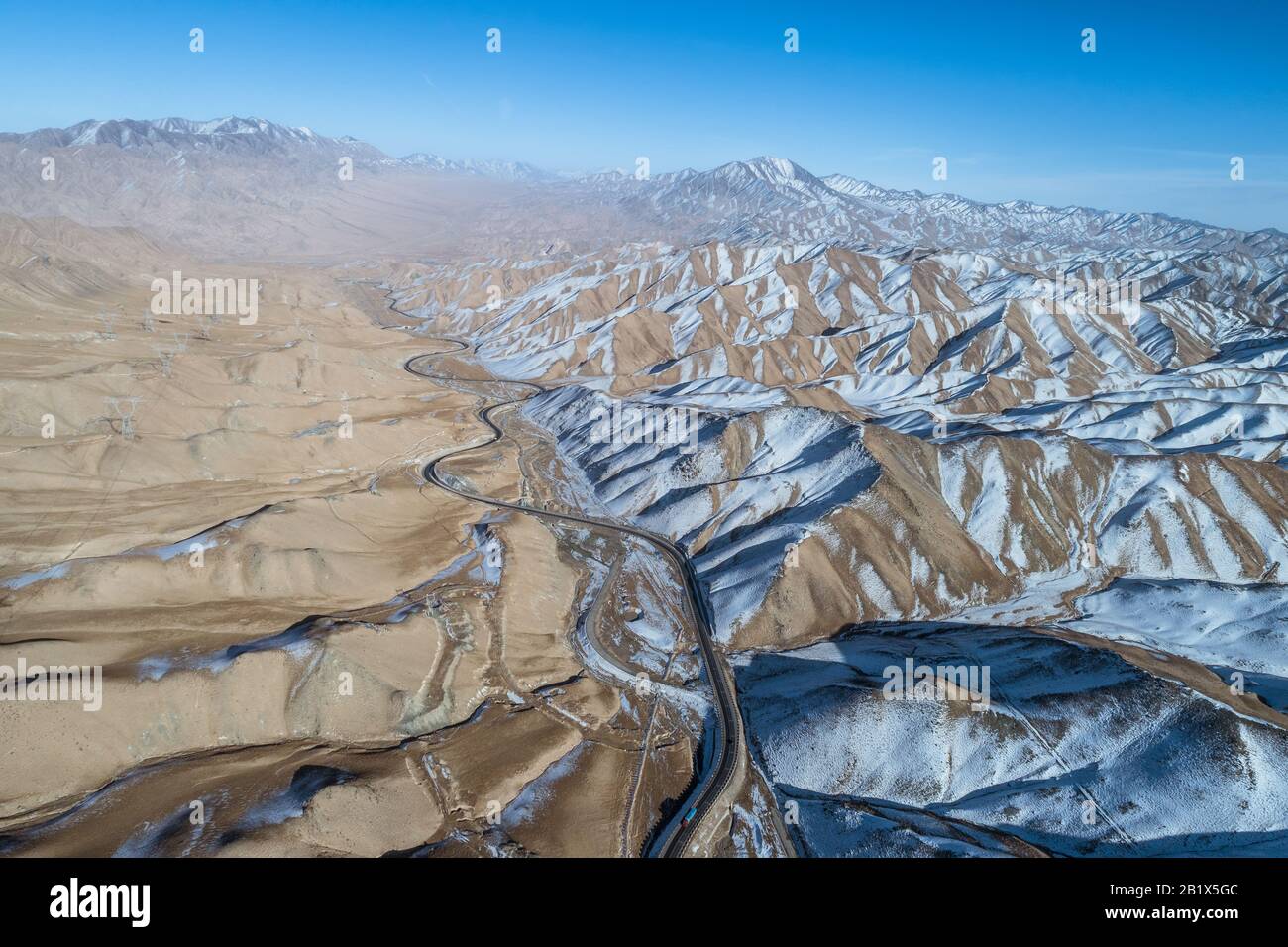 The country road winding through a valley surrounded by snowy mountains ...