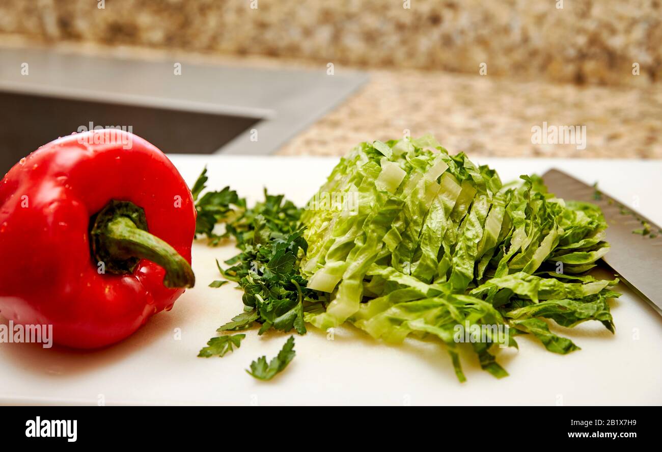A whole organic red pepper on a cutting board with organic romaine ...