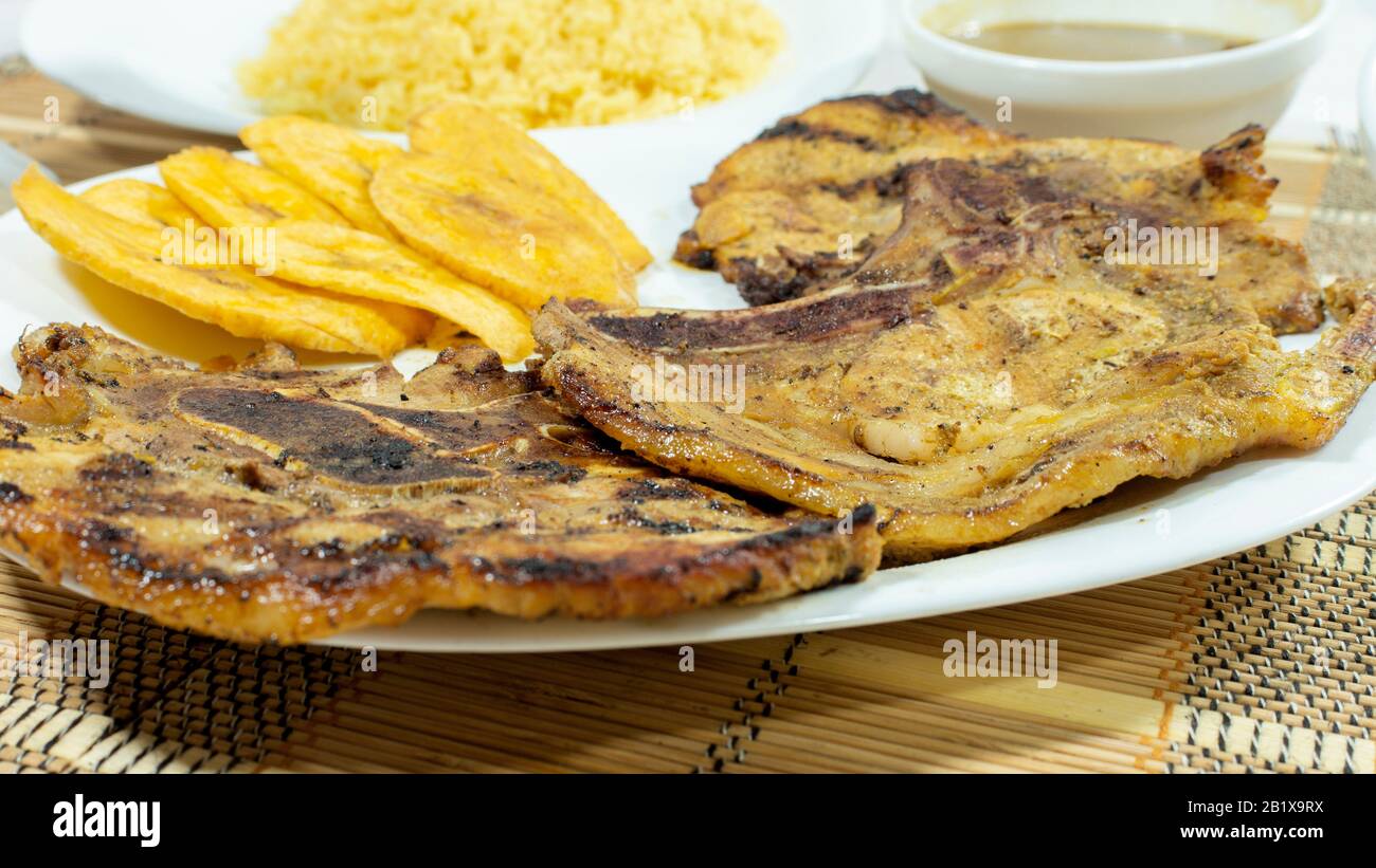White plate with pork chop accompanied by fried banana, yellow rice and ...