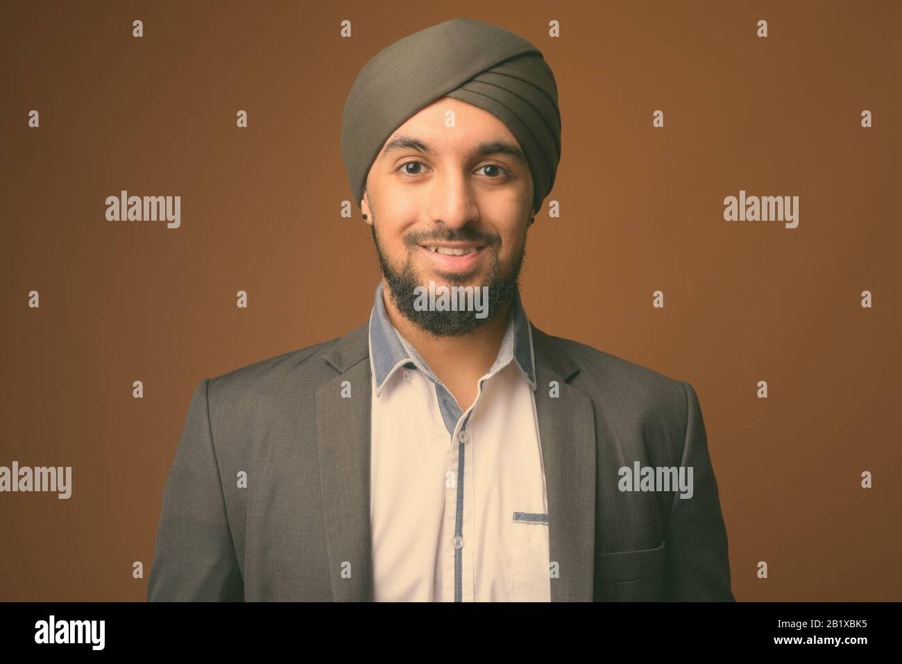 Studio shot of young bearded Indian Sikh businessman against brown ...