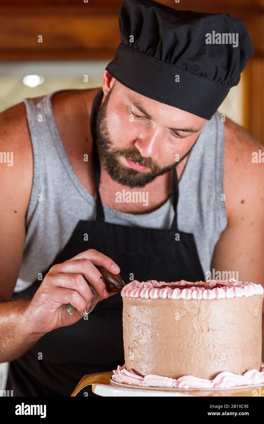 male baker decorating a chocolate birthday cake with strawberry moose ...