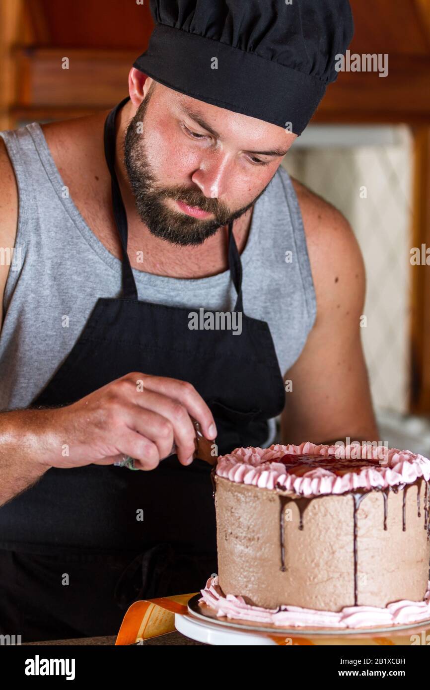 male baker decorating a chocolate birthday cake with strawberry moose ...