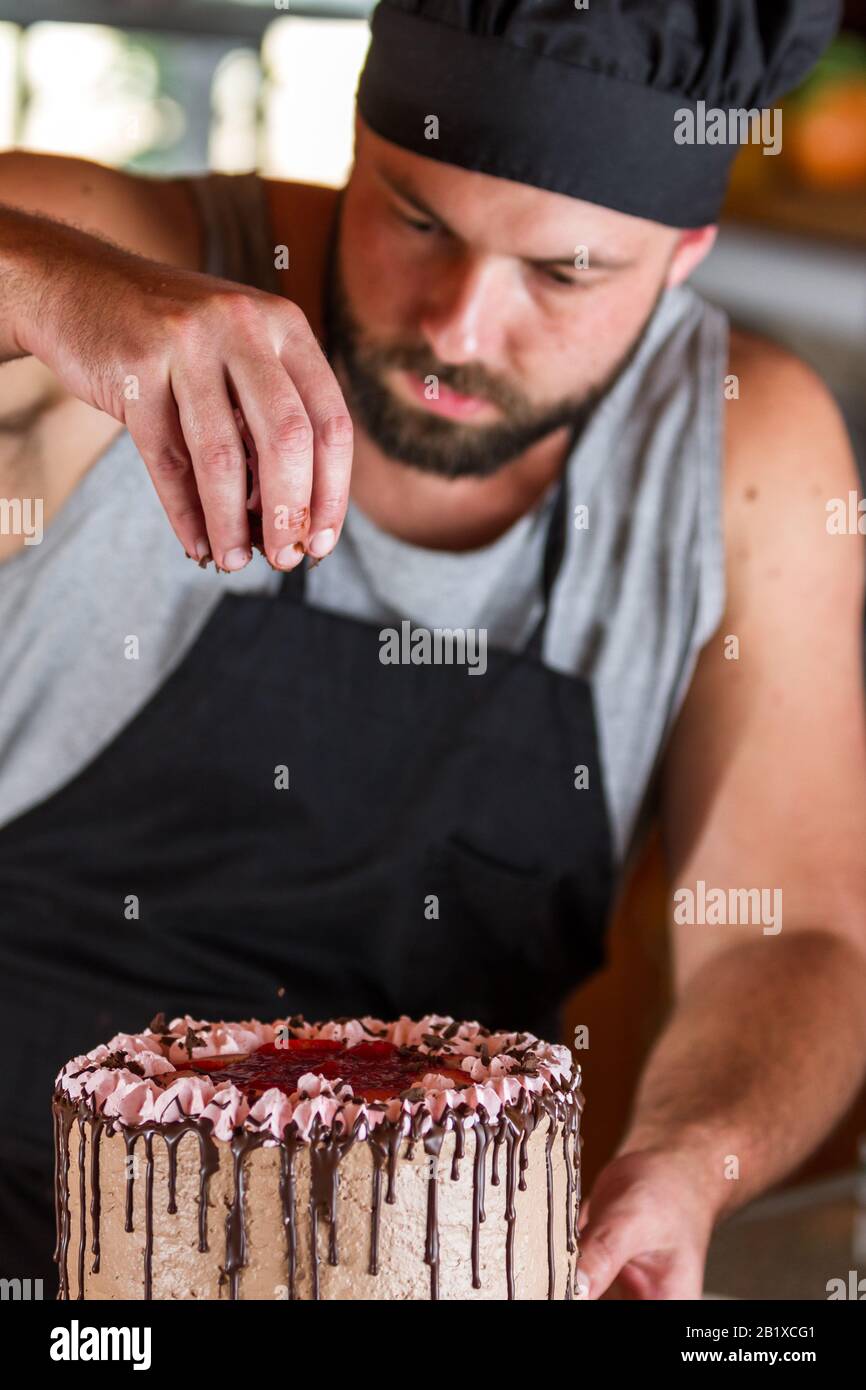 male baker decorating a chocolate birthday cake with strawberry moose ...
