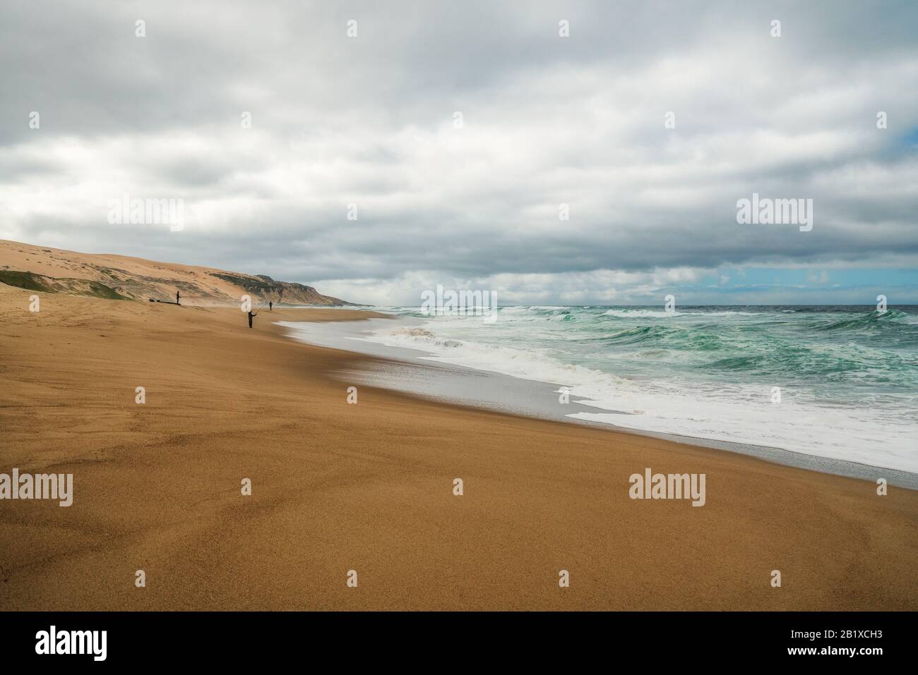 Wide sandy beach, stormy sea, beautiful cloudy sky, and silhouettes of ...