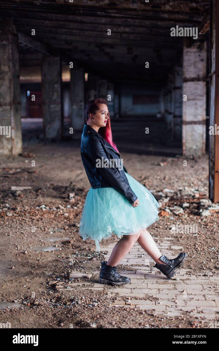 Portrait of a young girl with pink hair standing inside of collapsed ...