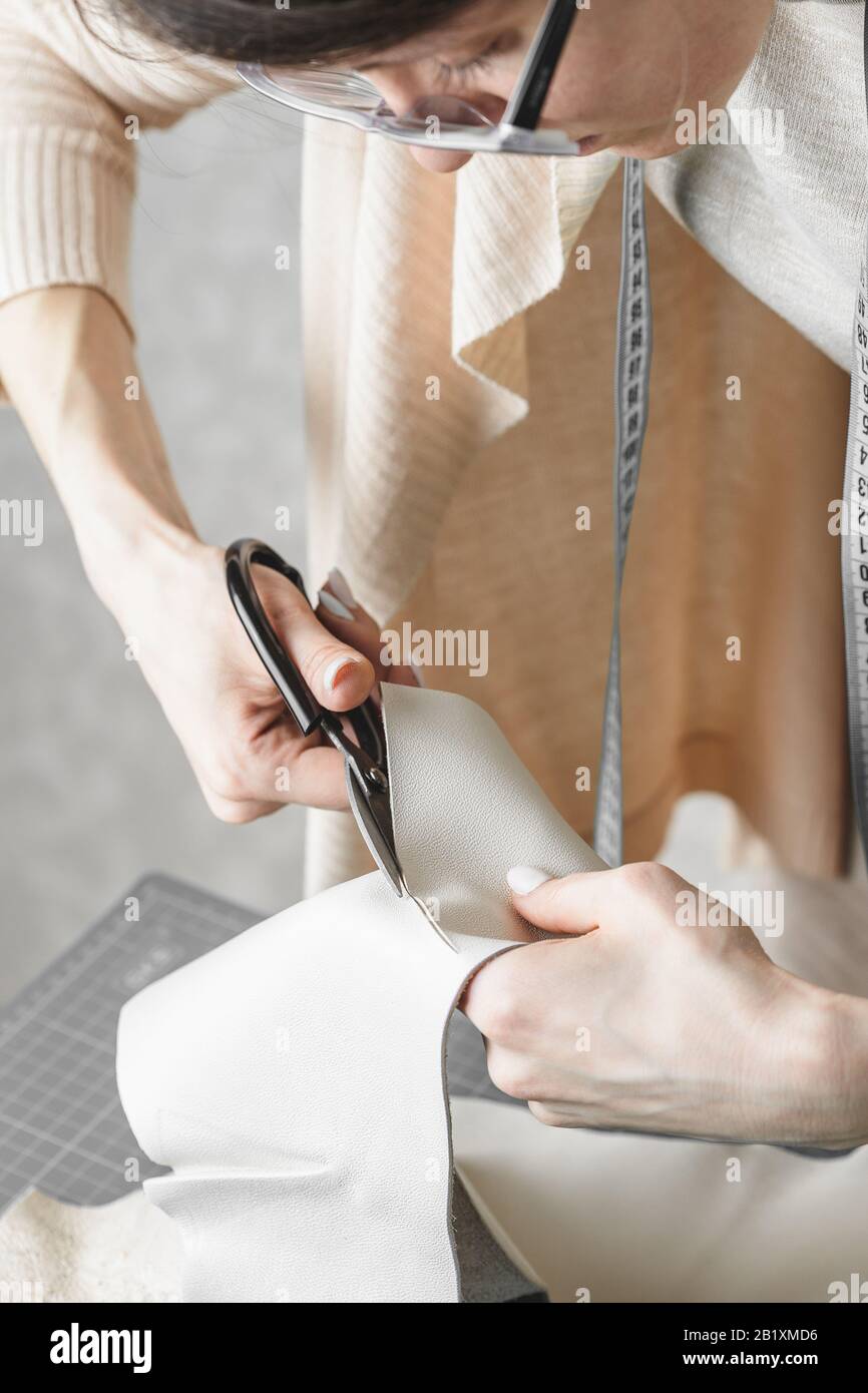 Female handbag designer measuring leather and cutting out details in a ...
